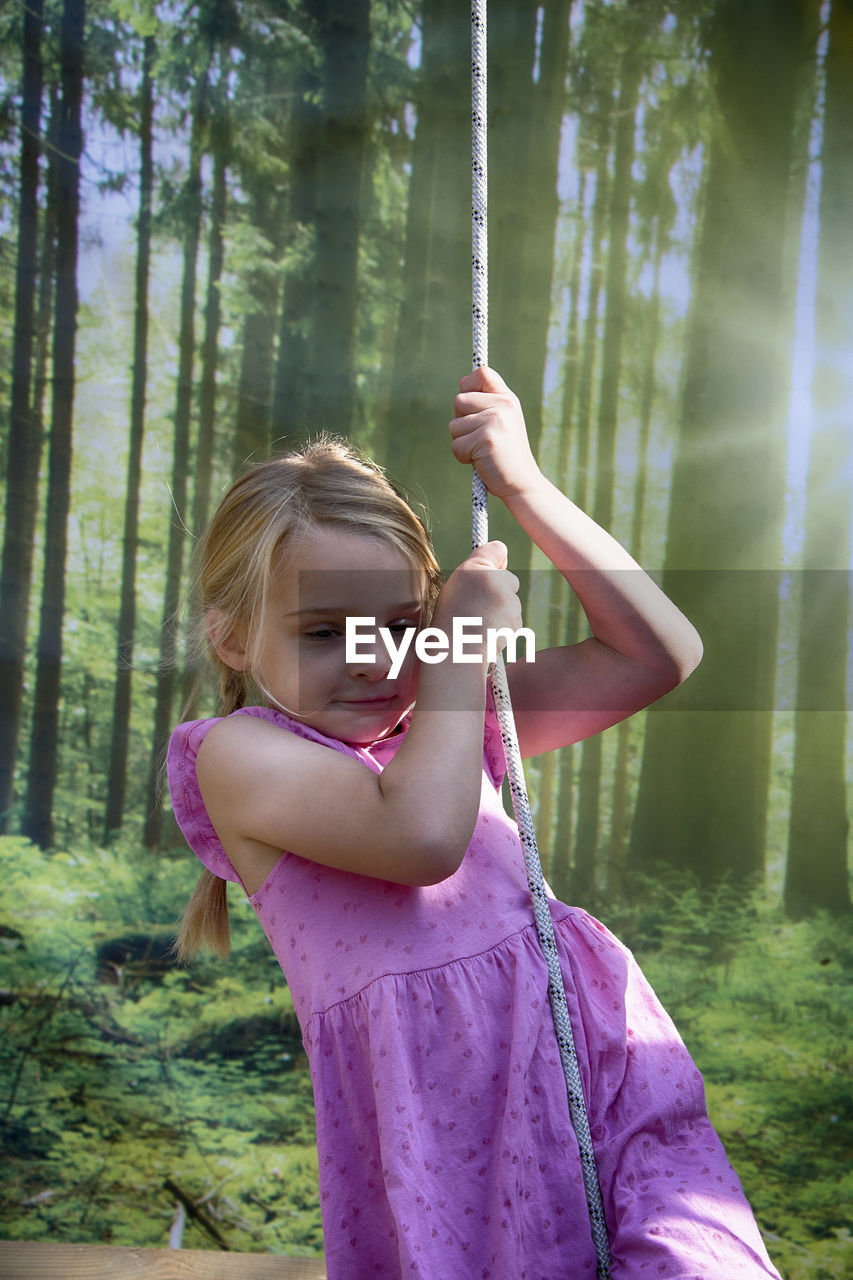 Girl hanging on rope against trees in forest | ID: 148367782