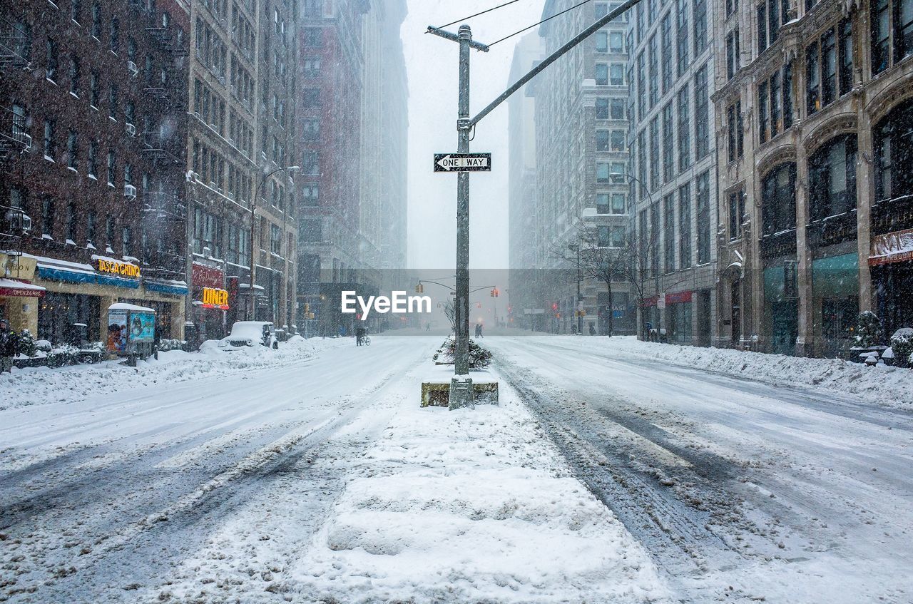 Street covered with snow amidst buildings in | ID: 79985007