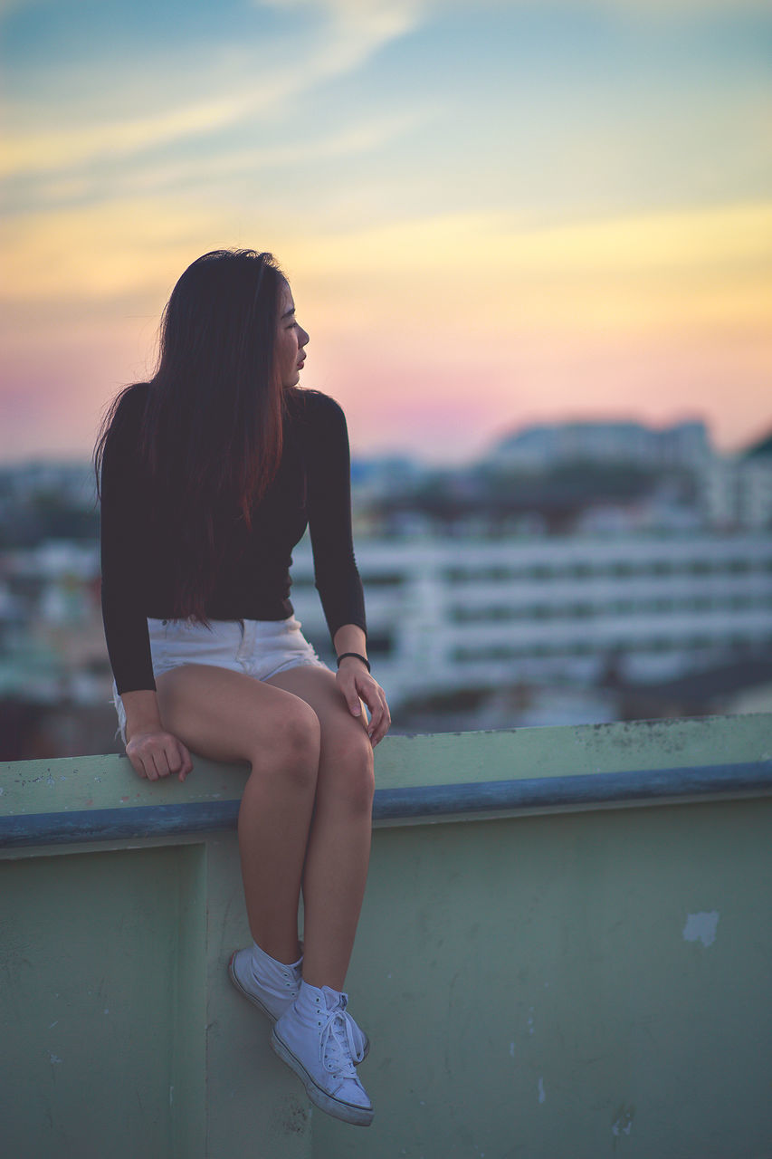 Woman sitting on railing during sunset | ID: 99333125