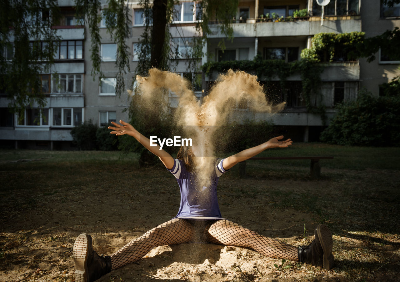 Woman throwing sand while sitting outdoors | ID: 149942883